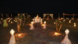 Decoração de casamento na praia, com um corredor enfeitado, velas e um bolo sobre uma mesa.