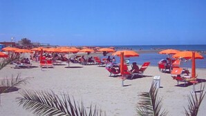 Uma praia com fileiras de guarda-sóis laranja e espreguiçadeiras.