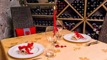 Mesa posta para dois com vela, taças de vinho e uma decoração em formato de coração vermelho.