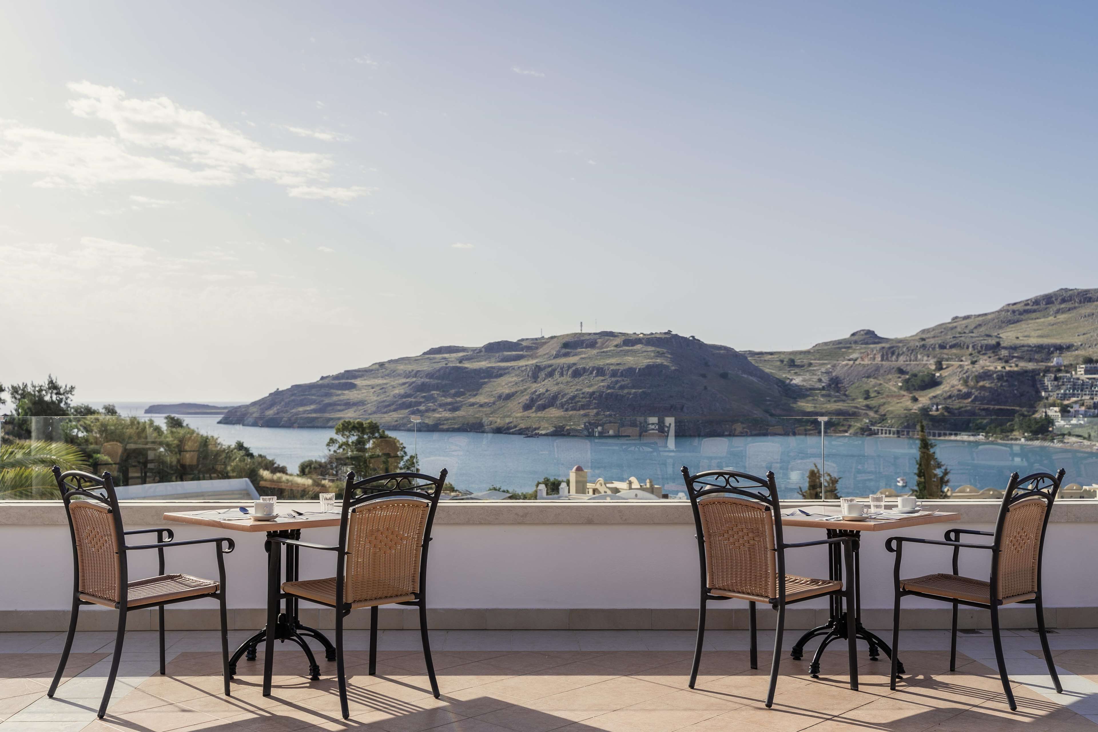 Terraço com mesa e cadeiras com vista para um lago e colinas.