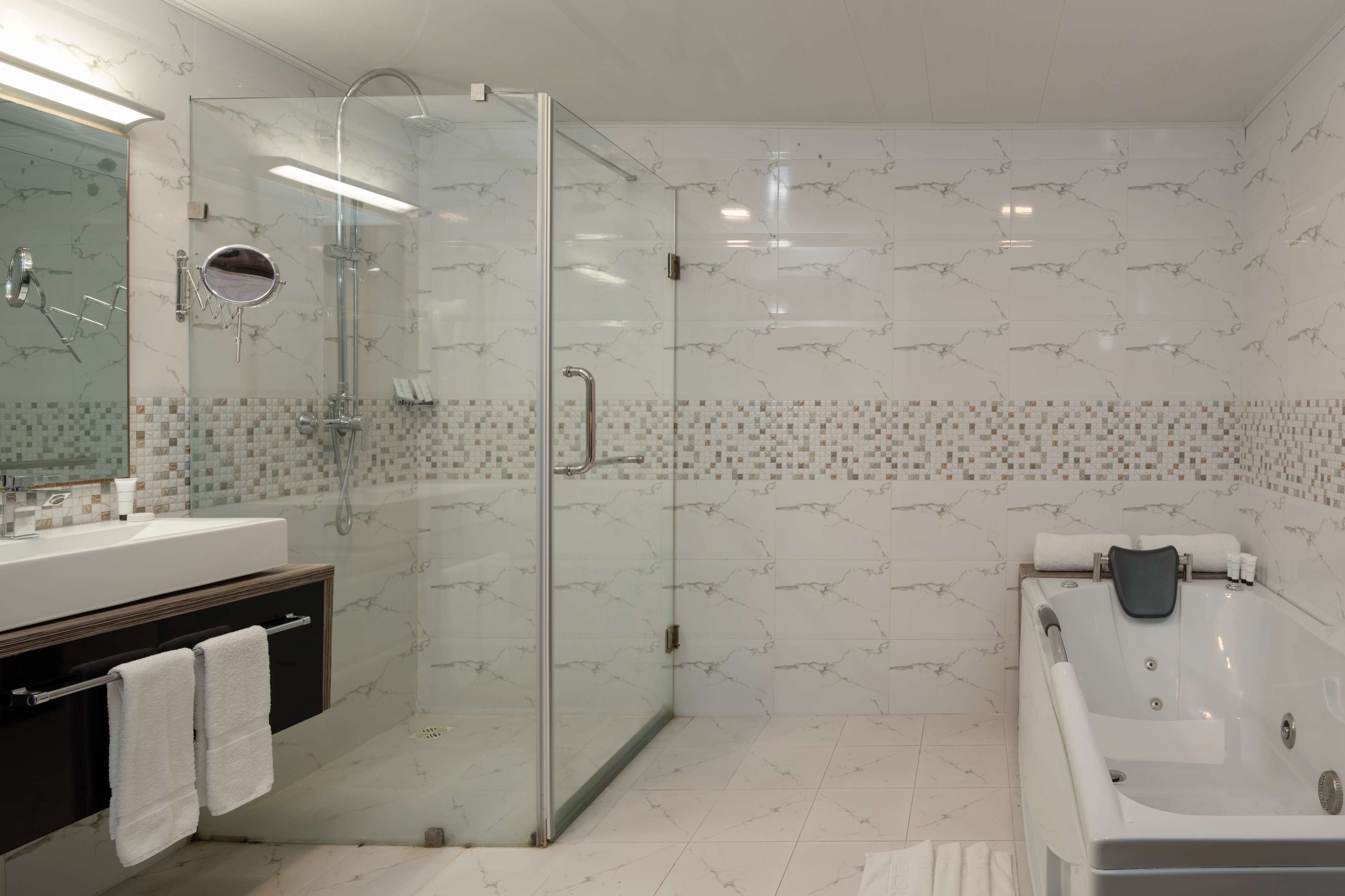 Uma casa de banho moderna com cabine de chuveiro em vidro, uma banheira grande e um lavatório com espelho e porta-toalhas.