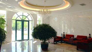 Um lobby com uma grande planta em vaso, sofás vermelhos e um candelabro.