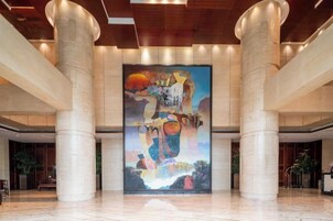 Um hall amplo com grandes colunas, um mural abstrato central e piso de mármore polido.
