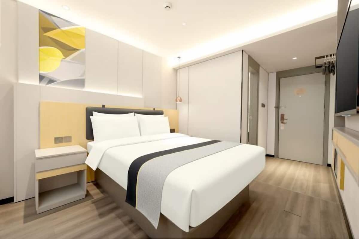 Quarto de hotel moderno com cama, mesas de cabeceira, televisão e guarda-roupa.