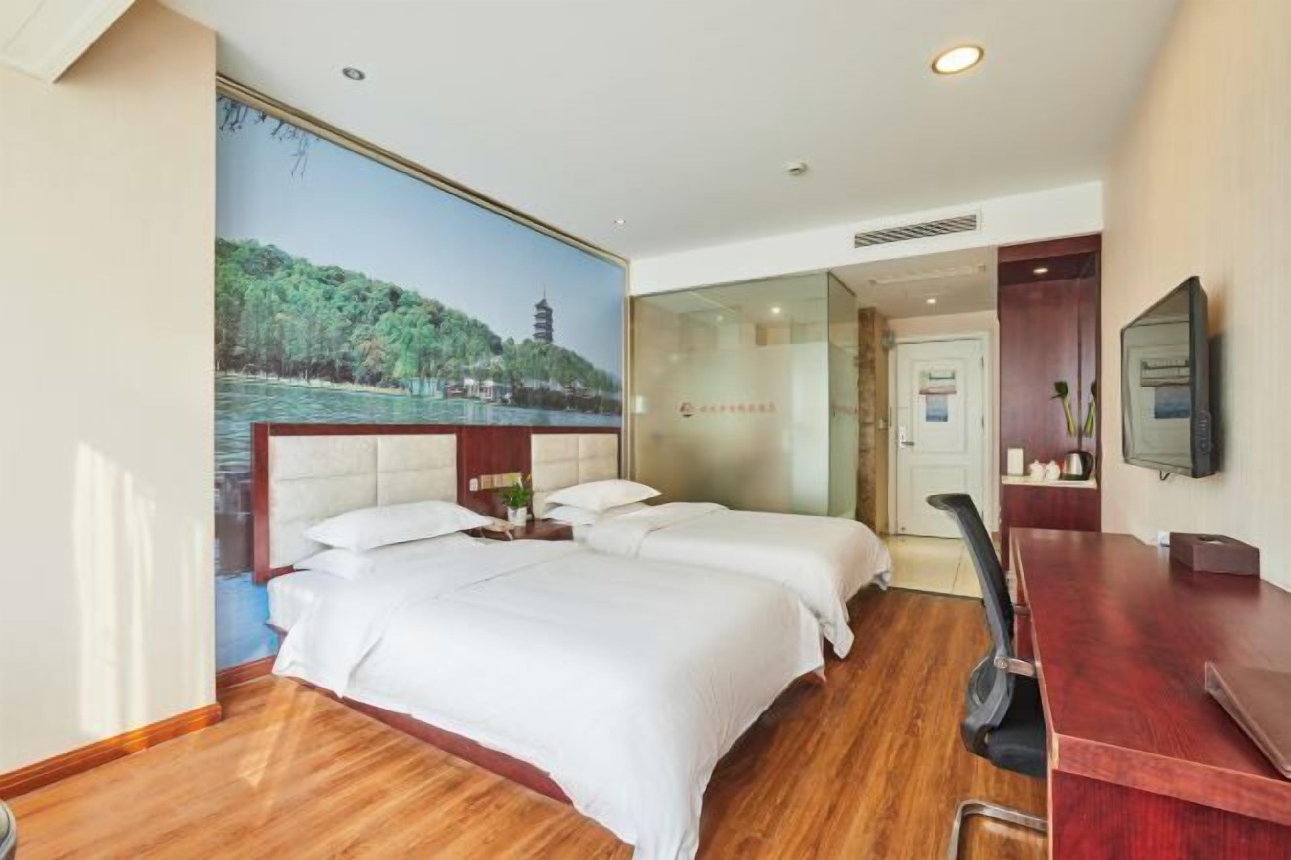 Quarto de hotel com duas camas, piso de madeira, grande janela com vista para um lago e um pagode, escrivaninha com cadeira e televisão na parede.