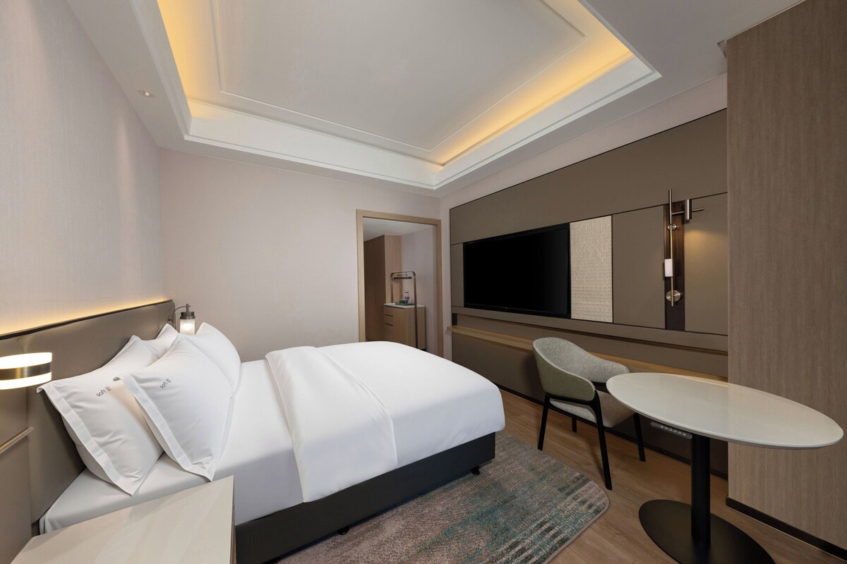 Quarto de hotel moderno com uma cama grande, escrivaninha, cadeira e televisão de tela plana.