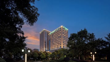 Um hotel moderno e imponente, cercado por vegetação e um pátio bem cuidado.