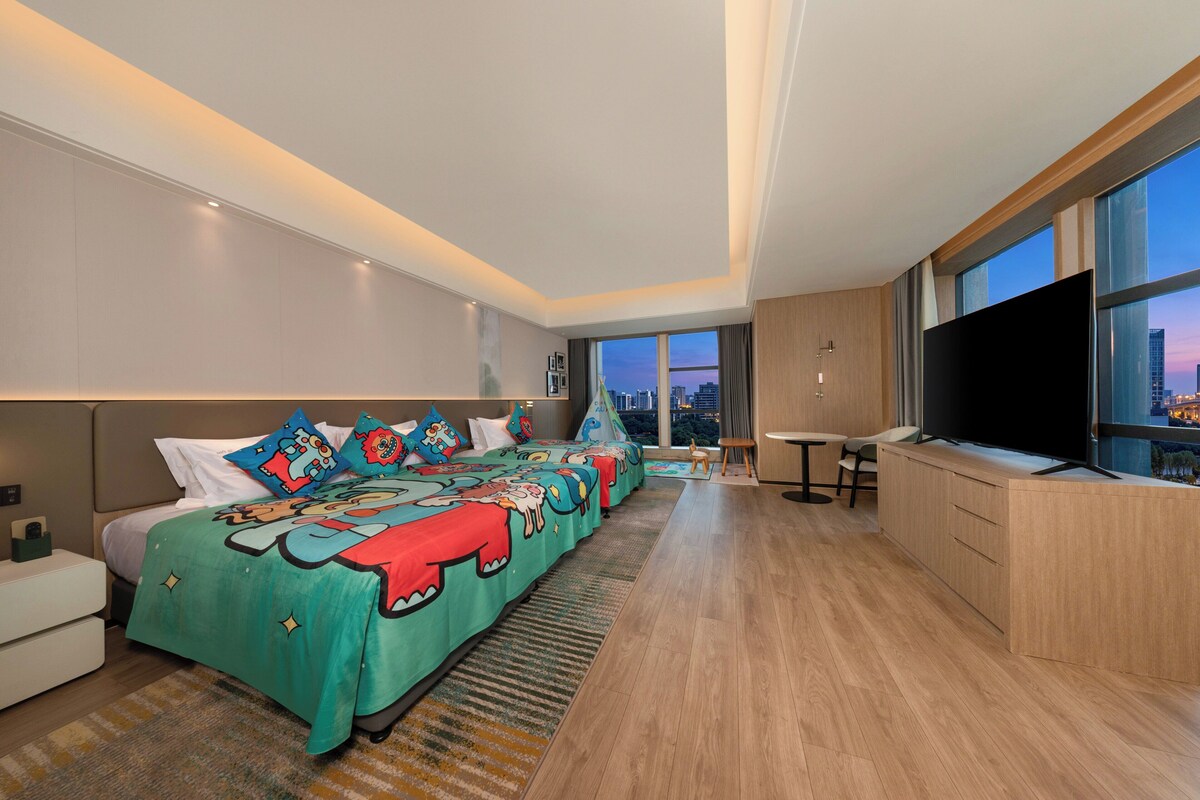 Quarto de hotel moderno com uma cama grande, uma escrivaninha, uma televisão e vista para a cidade.