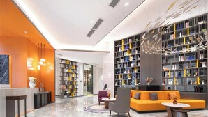 Uma biblioteca moderna com área de estar central, estantes de livros e um balcão de atendimento.
