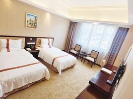 Quarto de hotel com duas camas, uma escrivaninha, uma cadeira e uma mesinha.