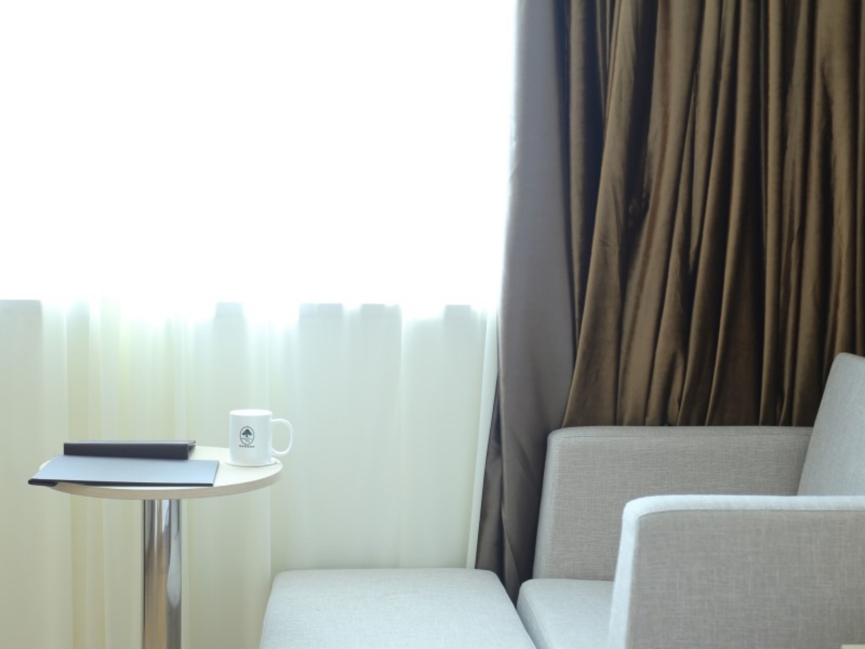 Quarto de hotel com uma pequena mesa, uma caneca branca e um sofá.