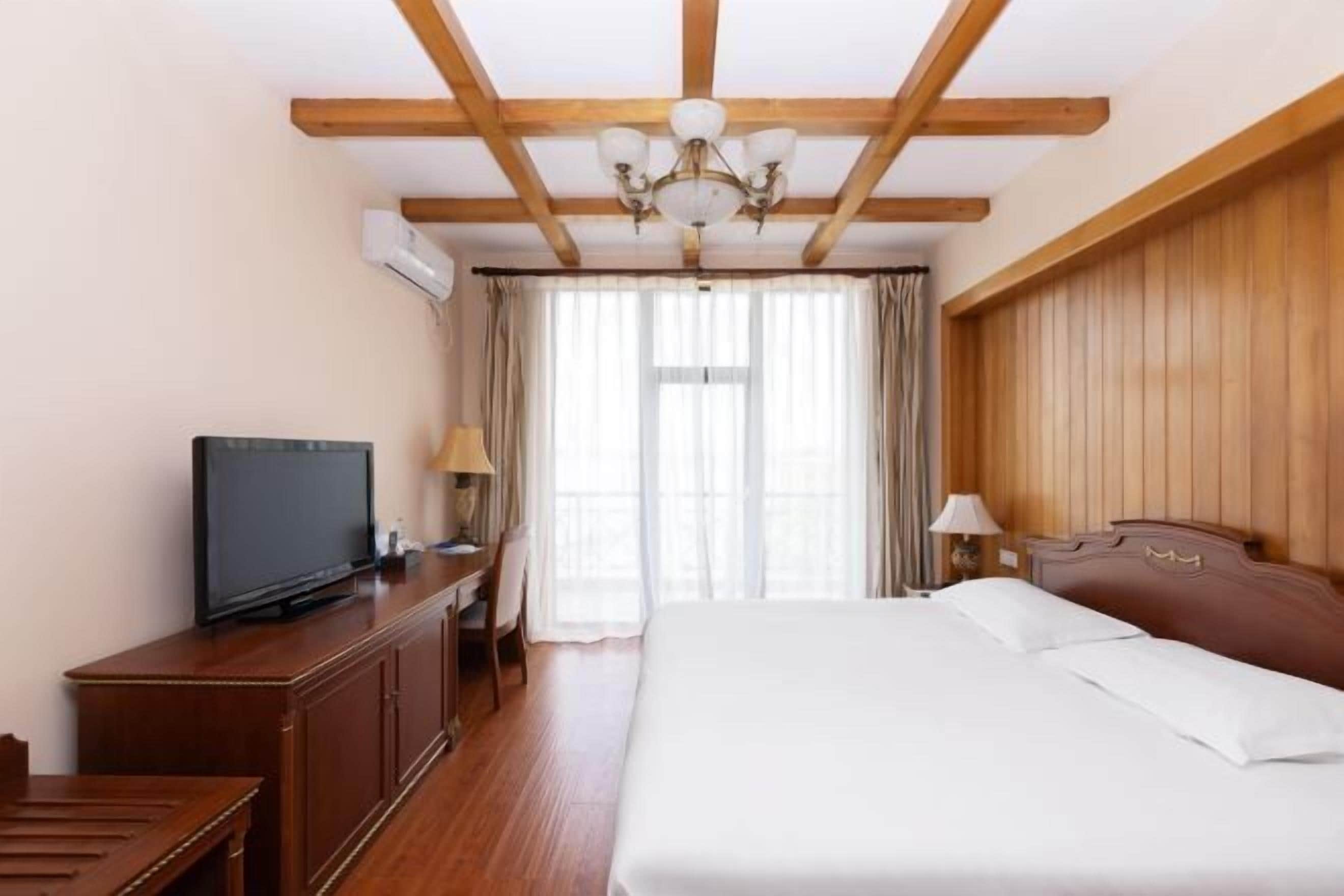 Quarto de hotel com cama, televisão, escrivaninha e cadeira.
