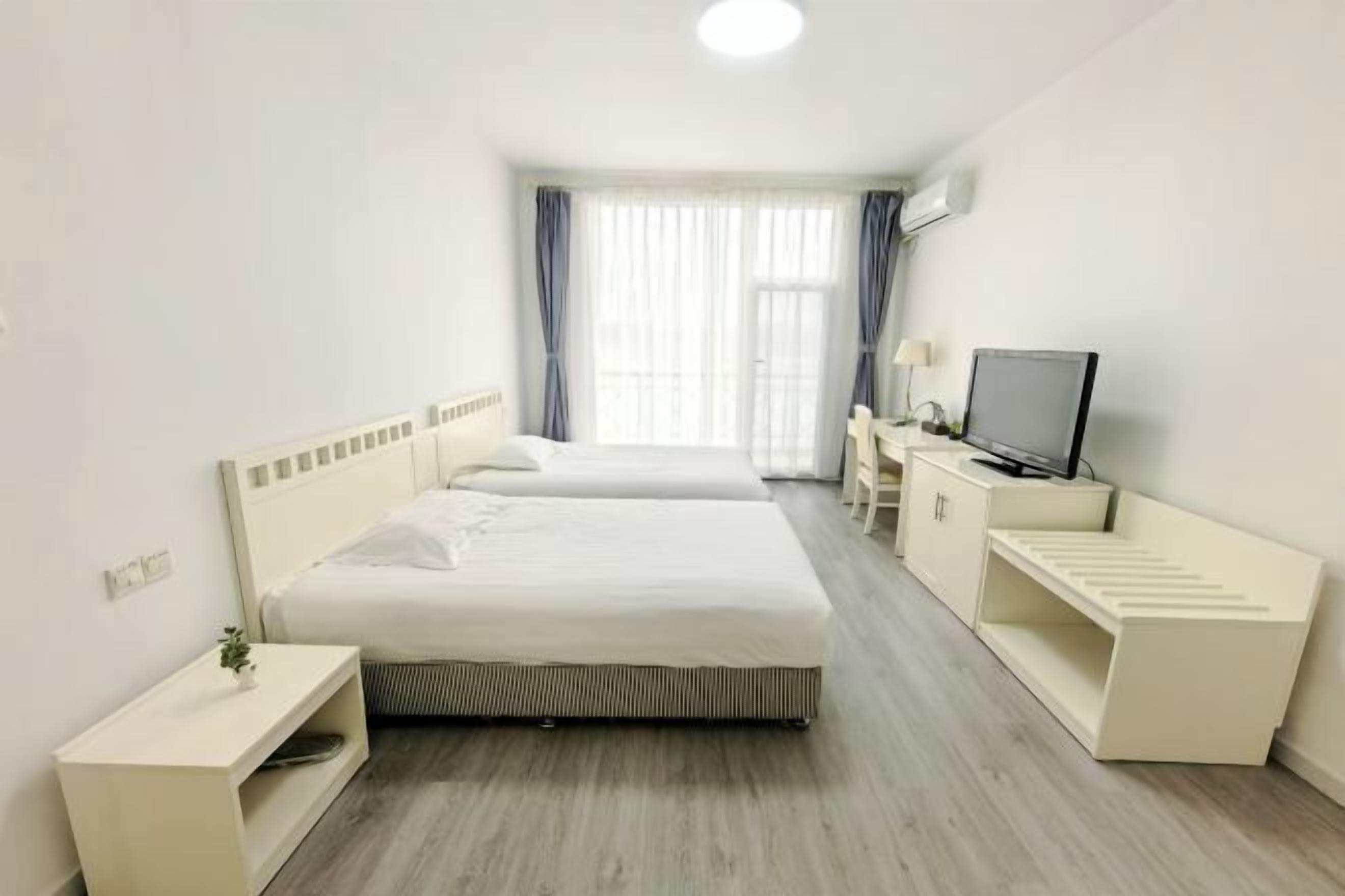 Quarto de hotel com duas camas, televisão, escrivaninha e janela com cortinas.