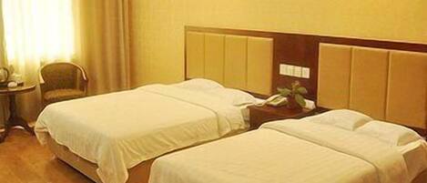 Quarto de hotel com duas camas, piso de madeira, mesa de cabeceira, uma cadeira e janela com cortinas.