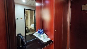 Quarto de hotel com guarda-roupa de madeira, bancada preta com chaleira e bandeja com garrafas e copos.