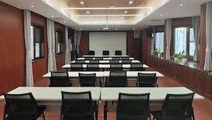 Sala de conferências com uma mesa comprida, cadeiras, uma tela de projetor e janelas com cortinas.