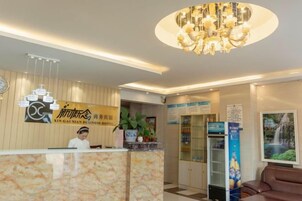 Uma área de recepção de hotel com balcão de mármore, um candelabro e um recepcionista.