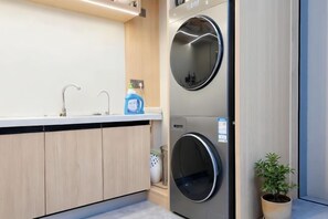 Uma lavanderia moderna com pia, duas máquinas de lavar empilhadas e um vaso de planta.