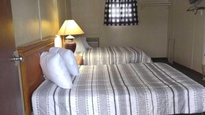 Quarto de hotel com duas camas, cada uma com roupa de cama listrada, uma luminária de cabeceira e uma persiana xadrez.