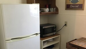 Uma cozinha compacta com uma geladeira branca, um micro-ondas e uma prateleira de madeira acima.