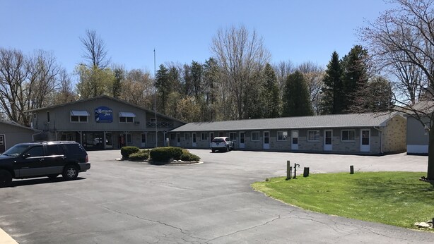 Um motel com estacionamento, um edifício com a placa "Maritime Inn" e uma área gramada com uma árvore.
