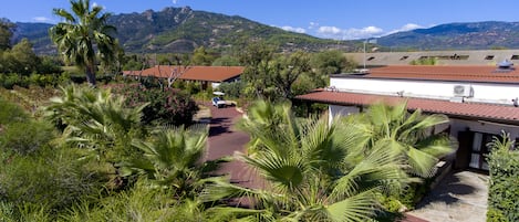 Área residencial com uma casa de telhado vermelho, um edifício branco também com telhado vermelho, e montanhas ao fundo.