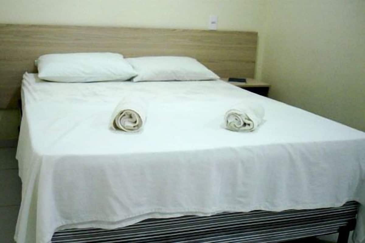 Cama bem arrumada com lençóis brancos e duas toalhas enroladas sobre a cama.