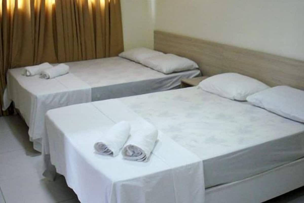 Quarto de hotel com duas camas de solteiro, cada uma com colcha e almofadas brancas, e cabeceira de madeira.