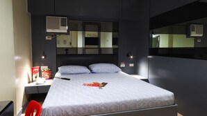 Quarto de hotel com cama, escrivaninha com cadeira, espelho e ar condicionado.