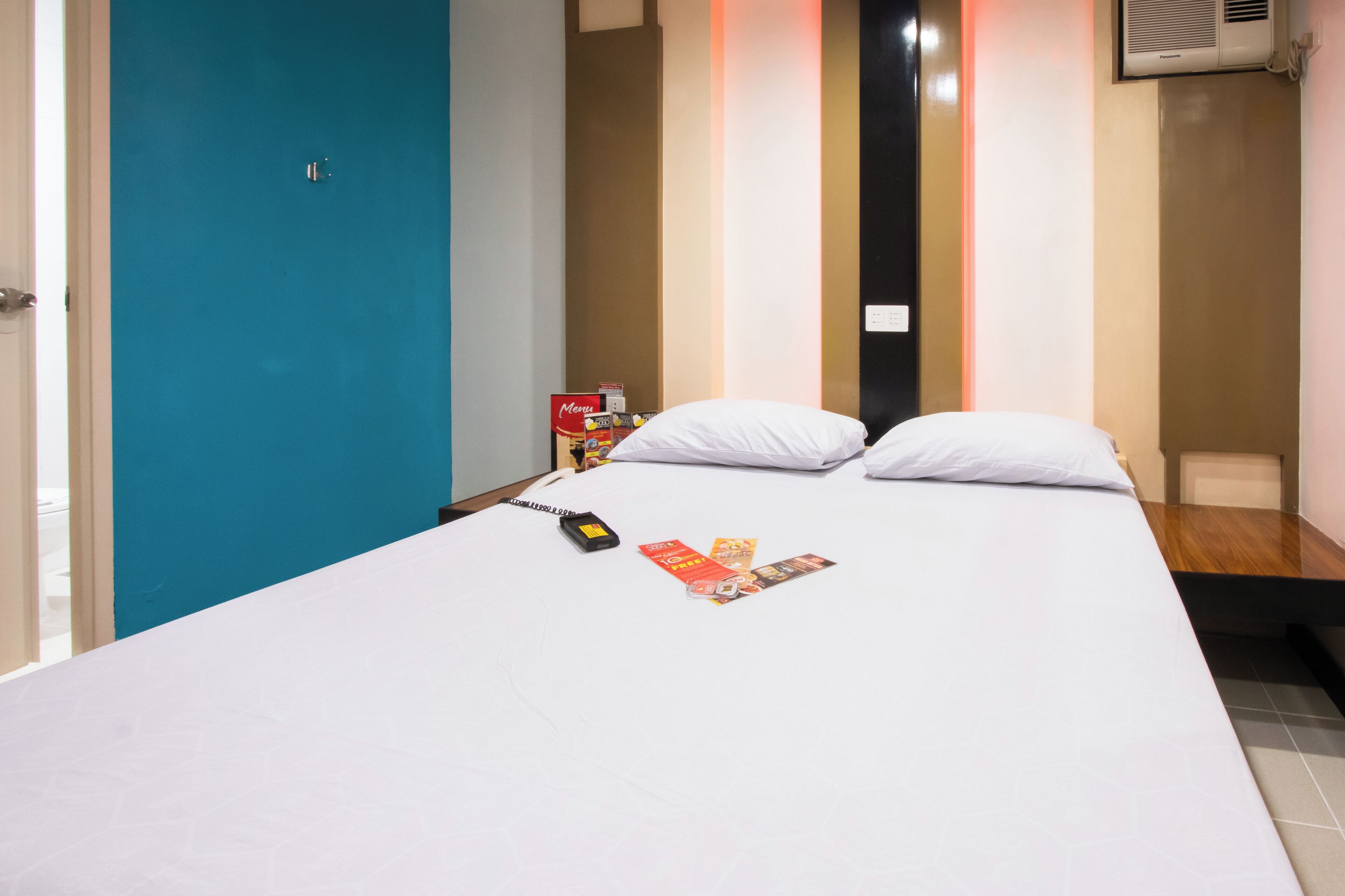 Quarto de hotel com cama, almofadas, mesa de cabeceira, telefone e revista.