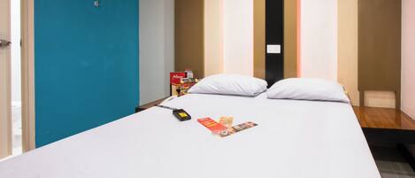 Quarto de hotel com cama, almofadas, mesa de cabeceira, telefone e revista.