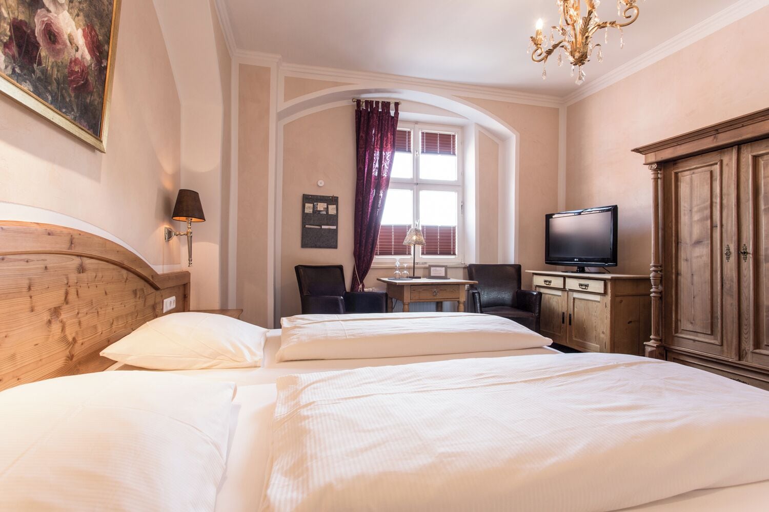 Quarto de hotel com uma cama grande, uma escrivaninha com cadeira, uma televisão e um guarda-roupa.