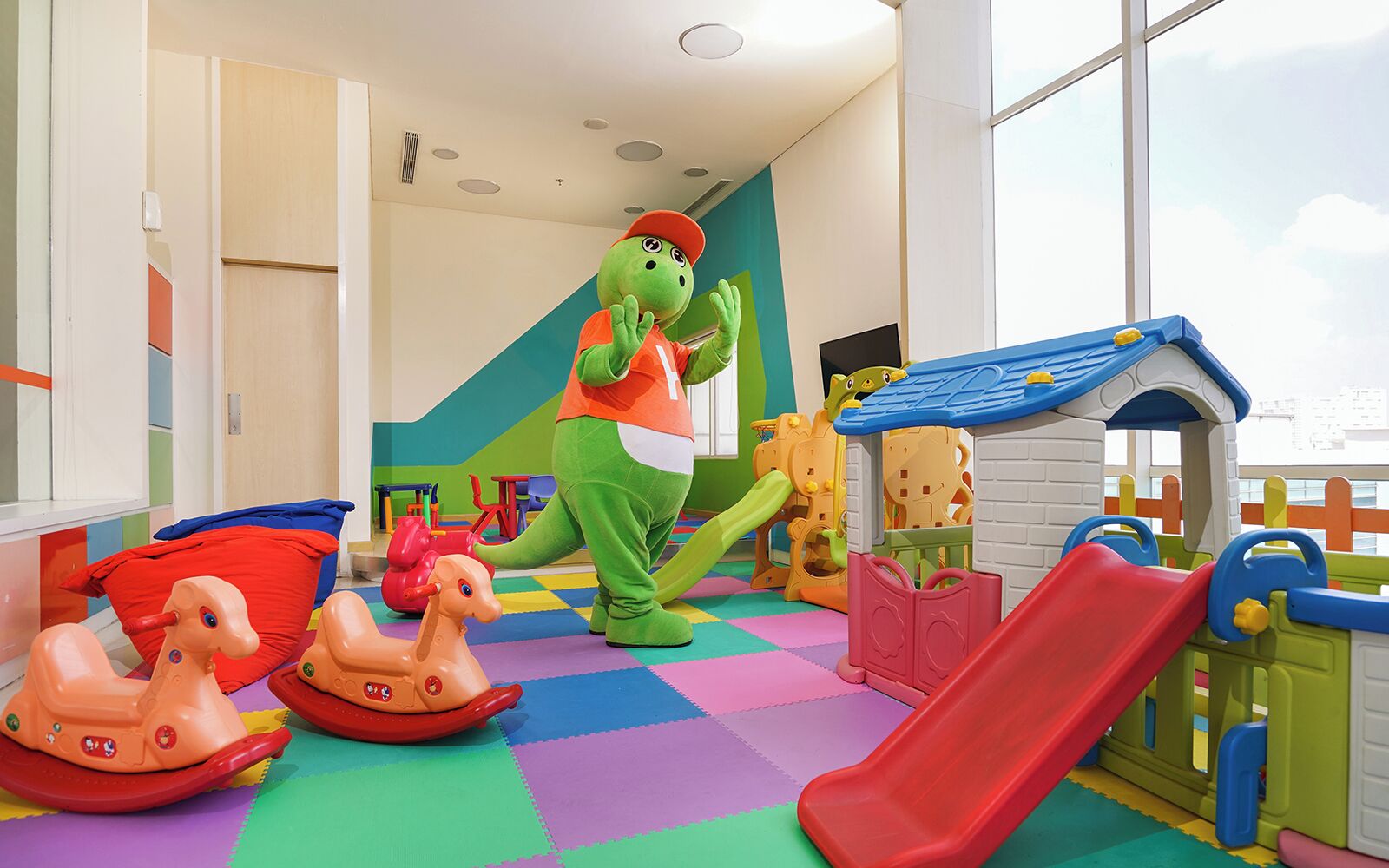 Uma área de recreação com um mascote de dinossauro, brinquedos coloridos e um escorregador.