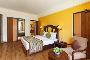 Quarto de hotel com cama, mesa de cabeceira, cadeira e uma pequena mesa com um vaso de flores.