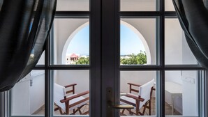 Varanda com duas cadeiras de madeira e uma mesa, com vista para um prédio e vegetação.