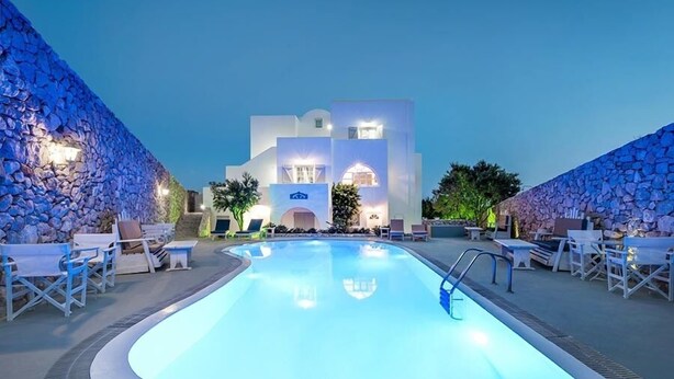 Piscina com espreguiçadeiras e um edifício com paredes de pedra e iluminação.
