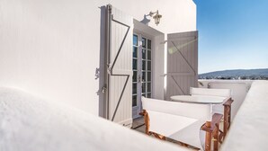 Uma área de estar ao ar livre com mesa e cadeiras, uma porta e vista para a paisagem.