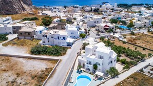 Vista aérea de uma vila costeira com edifícios brancos, uma piscina e uma estrada.
