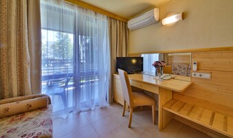 Quarto de hotel com secretária de madeira, televisão, sofá e janela com cortinas.