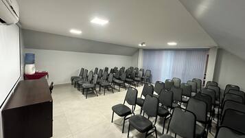 Sala de conferência com fileiras de cadeiras, um púlpito e um bebedouro.