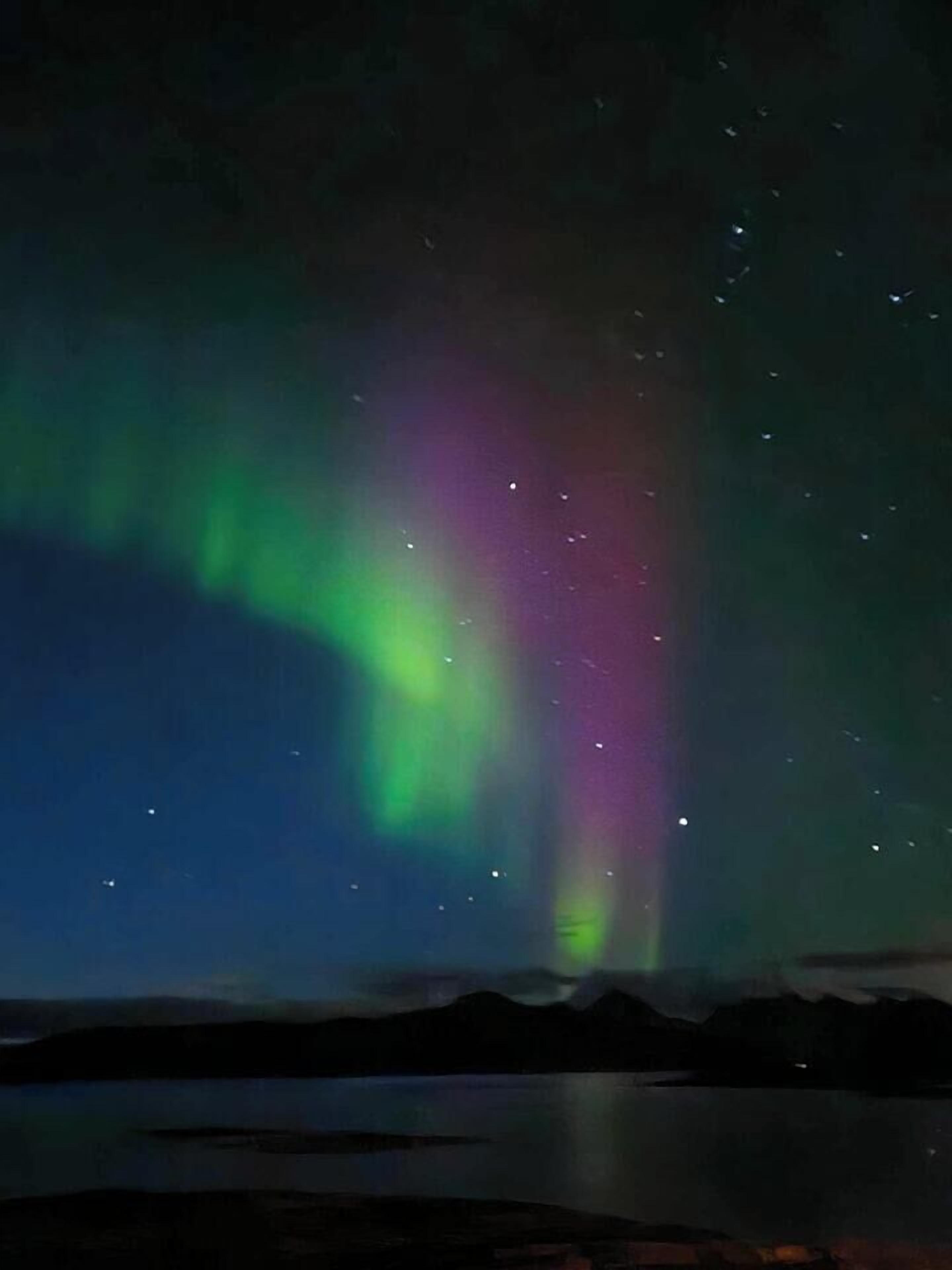 Céu noturno com auroras boreais sobre uma paisagem montanhosa.