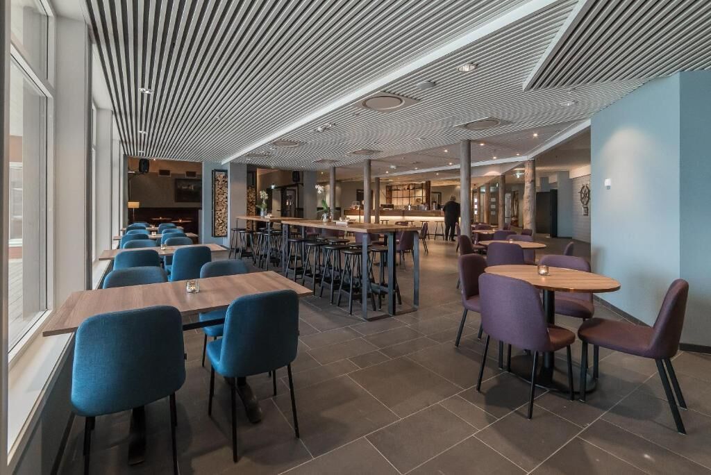 Um restaurante moderno com teto alto e área de bar. Mesas e cadeiras dispostas para refeições.