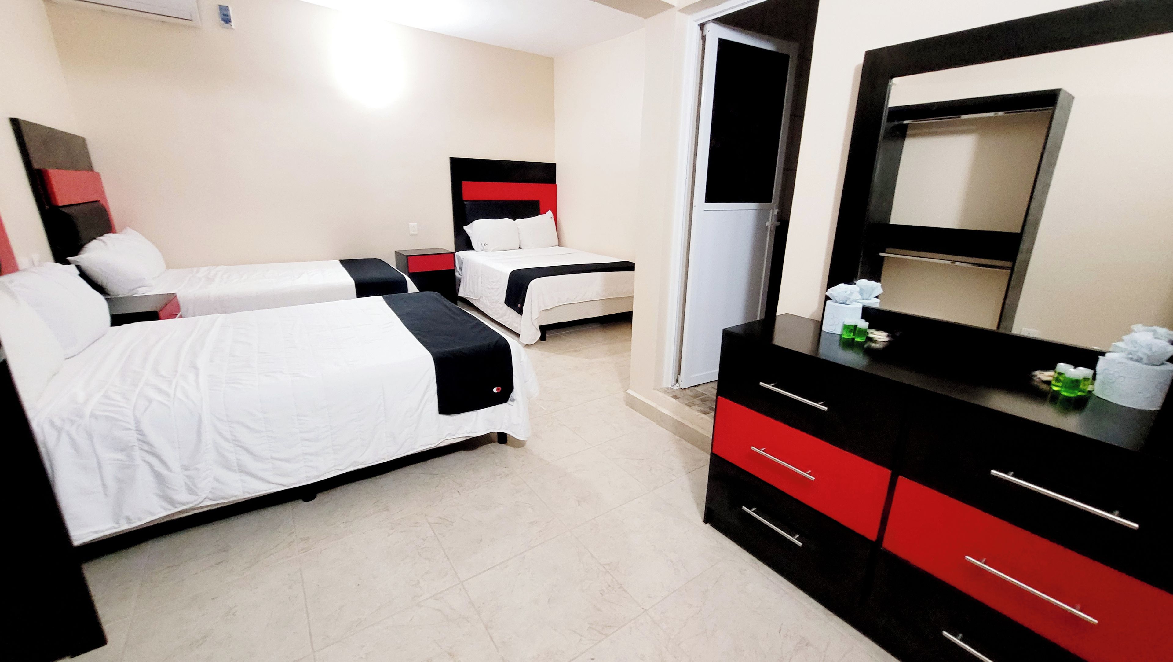 Quarto de hotel com duas camas, uma cômoda preta e vermelha e um espelho.