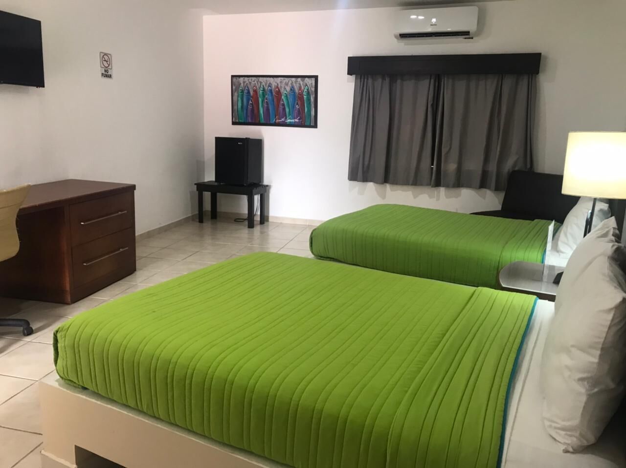 Quarto de hotel com duas camas, uma escrivaninha, uma cadeira, uma televisão e um quadro na parede.