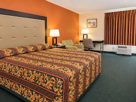 Quarto de hotel com uma cama grande, duas cadeiras, uma escrivaninha e uma janela com cortinas.