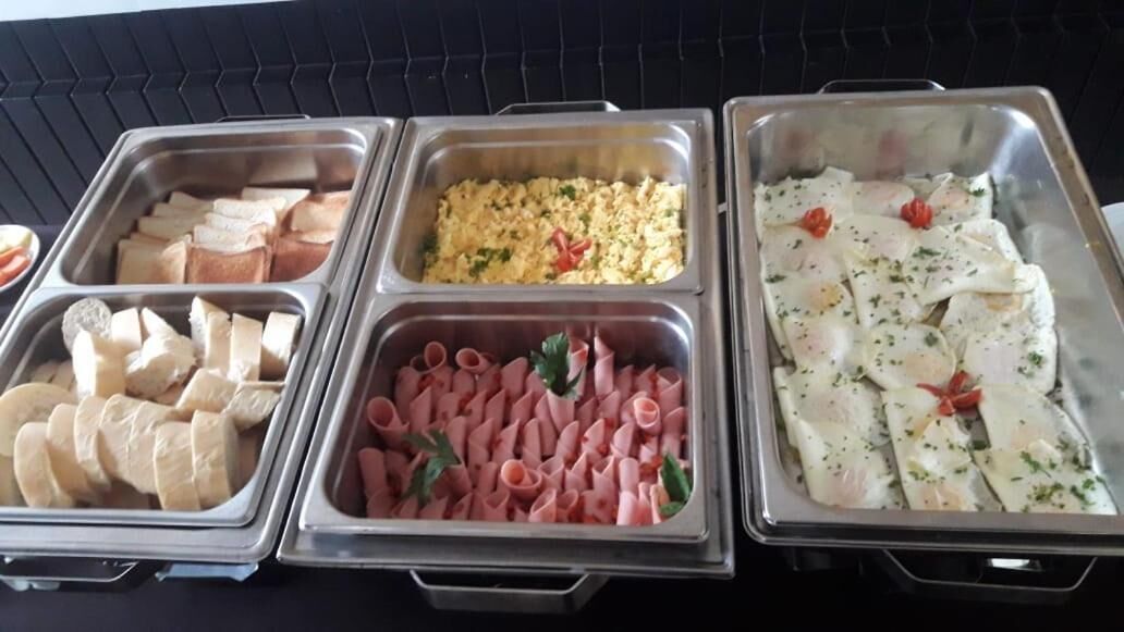 Buffet com diversos alimentos, incluindo pão, ovos, presunto e peixe.
