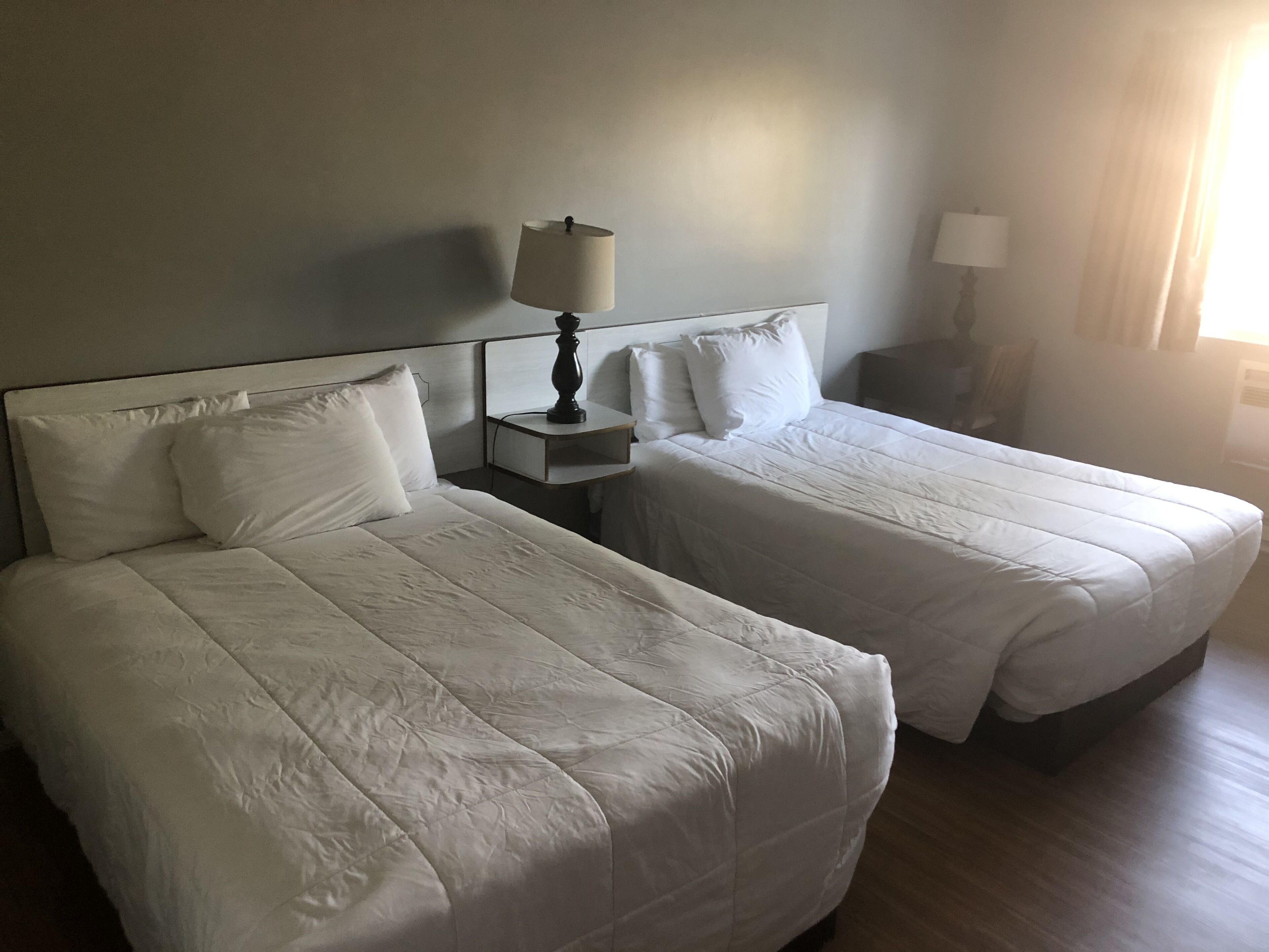 Quarto de hotel com duas camas, uma mesa de cabeceira, uma luminária e uma cadeira.
