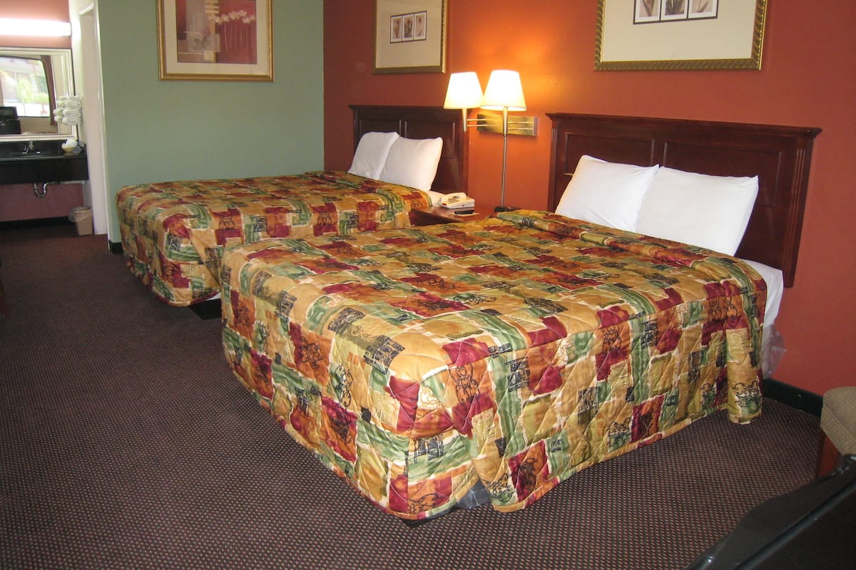Quarto de hotel com duas camas, uma escrivaninha e um espelho.
