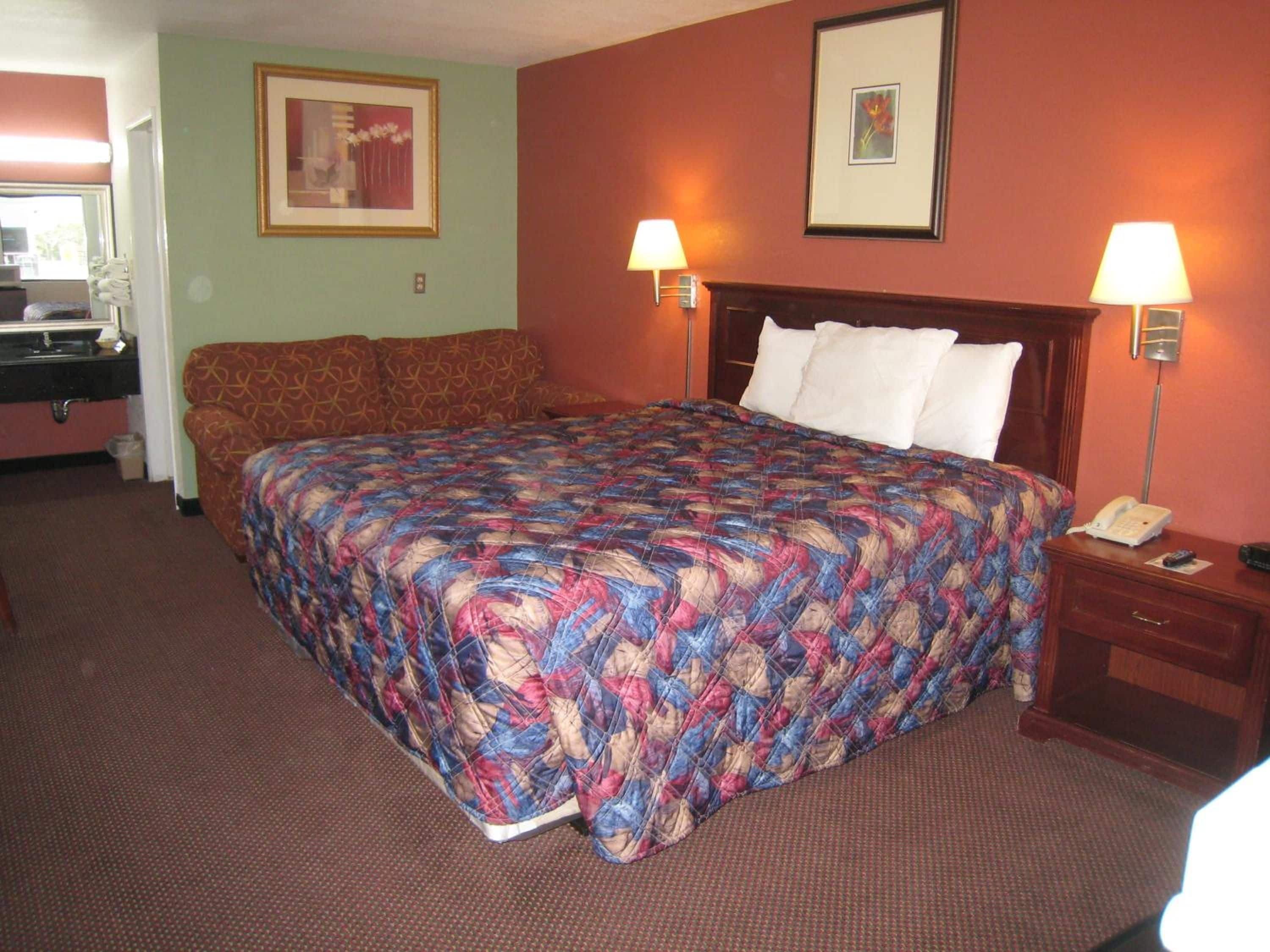 Quarto de hotel com uma cama grande, duas luminárias de cabeceira, mesa de cabeceira com telefone e quadro na parede.