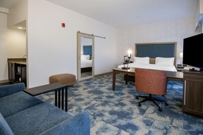 Quarto de hotel com cama, escrivaninha, cadeira e televisão.